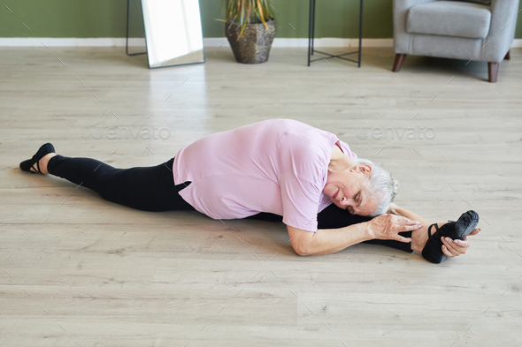 Active and flexible senior female keeping head on stretched leg during ...