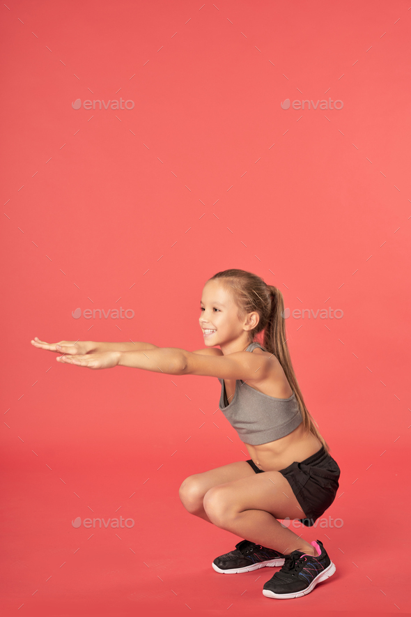 Cheerful female child in sportswear doing squats Stock Photo by friends ...