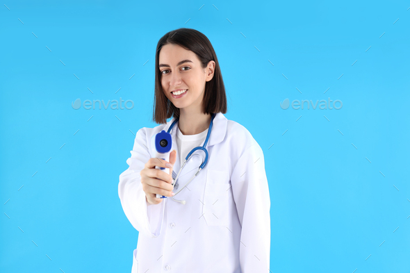 Female trainee doctor with thermometer gun on blue background Stock ...