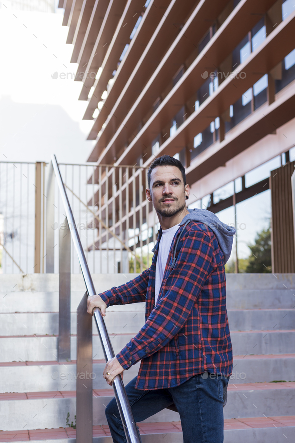 young man standing and looking away with arms leaning on railing ...