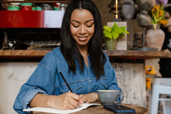 Smiling young african woman writing in notebook Stock Photo by vadymvdrobot