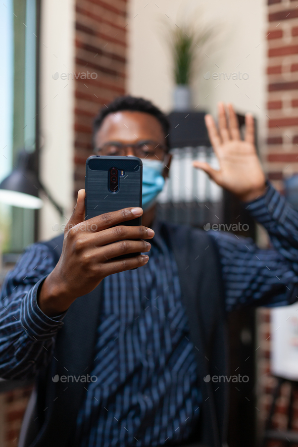 Closeup of smartphone of startup employee wearing face mask waving ...