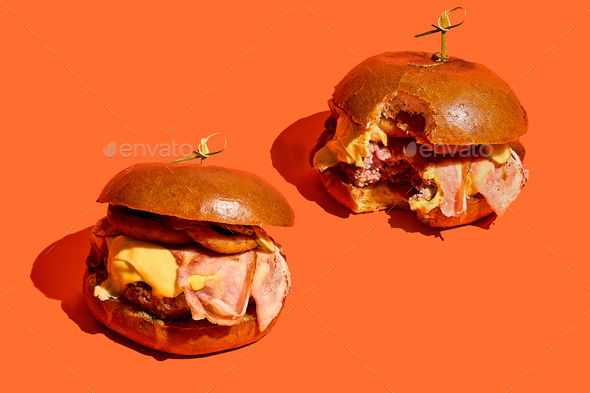 Two burgers with bacon and onions, melted cheese. One bitten burger on ...