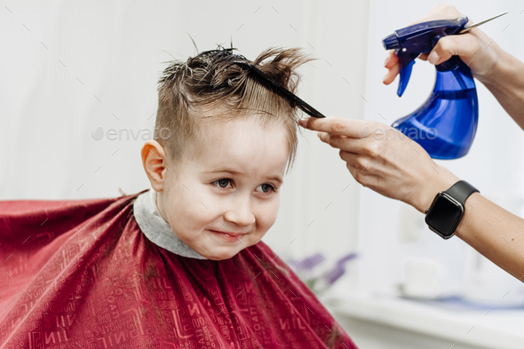 Barber's hands spray the little boy's hair with a spray gun. Stock ...
