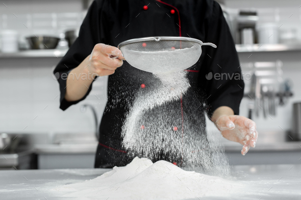 The pastry chef's hands sift the flour through a sieve on the table ...