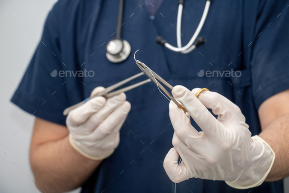 Doctor holds, in hand with disposable glove, forceps and needle holder ...