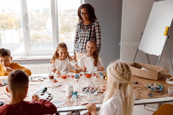 Smiling classmates painting on paper with colorful paints in school ...
