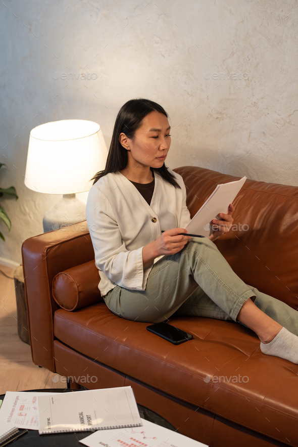 Young serious Asian female auditor looking through financial documents ...