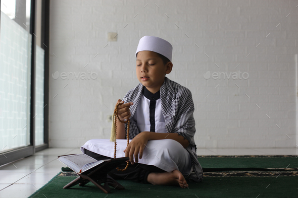 Muslim boy praying using prayer beads Stock Photo by Garakta-Studio