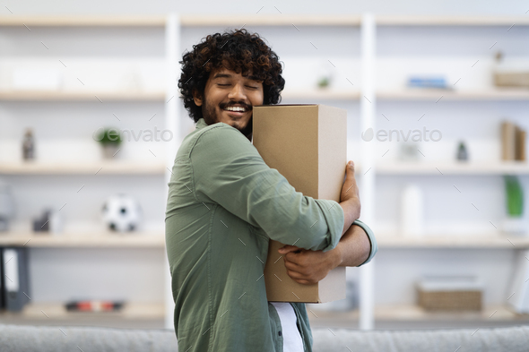 Ecstatic young indian man hugging box at home Stock Photo by Prostock ...