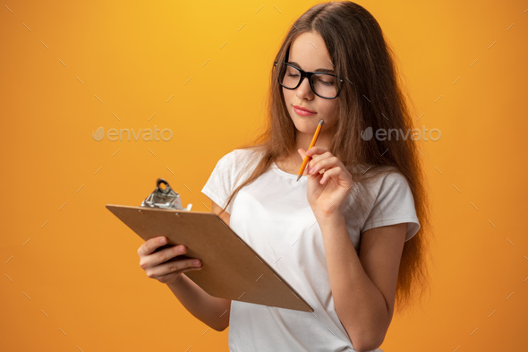 Teen school girl taking notes on clipboard against yellow background ...