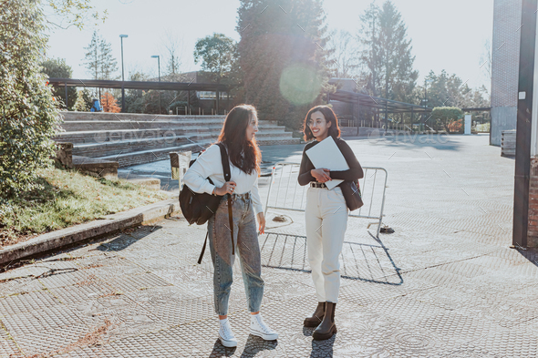 Two young student woman going to class while talking and laughing ...