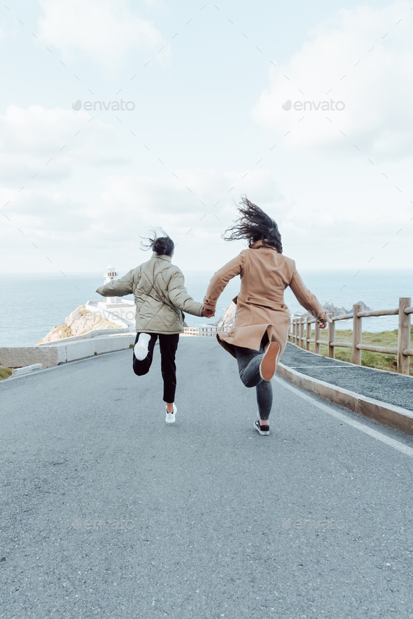 Two Young girls running together holding hands towards the seashore and ...