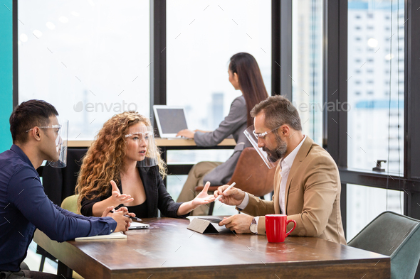 Male manager in face shield explaining work project to colleagues in ...