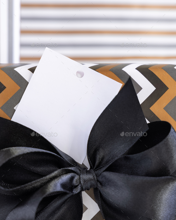 Wrapped present with blank square gift tag and black bow close up ...
