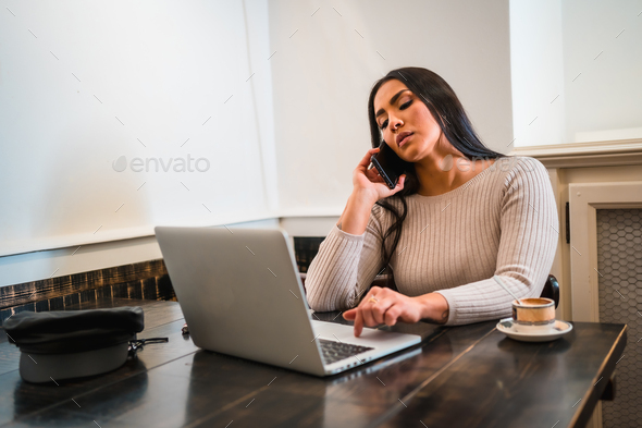 Brunette girl teleworking in a cafeteria with laptop, making a work ...