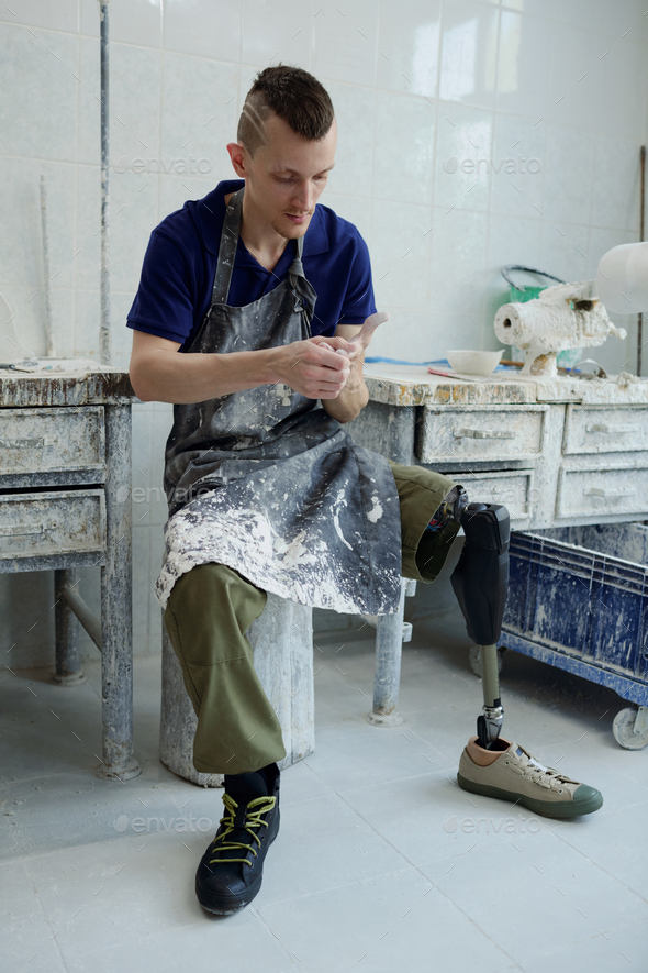Young restful man with disability sitting by small table in prosthetic ...