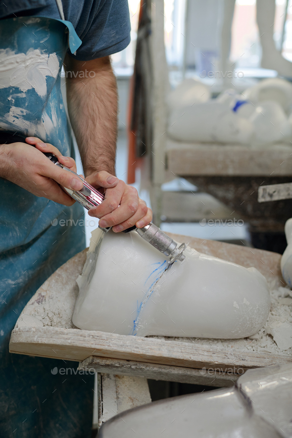 Hands of young manufactory worker cutting part of plaster cast Stock Photo by Pressmaster