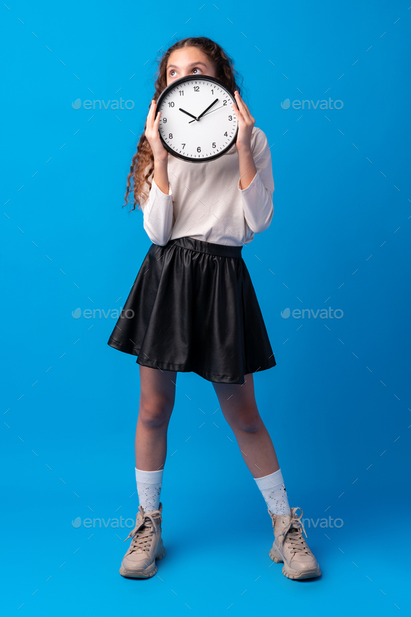 Beautiful teen girl holding wall clock over blue background Stock Photo ...