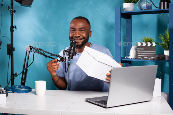 Smiling vlogger holding white box in vlogging studio with professional ...