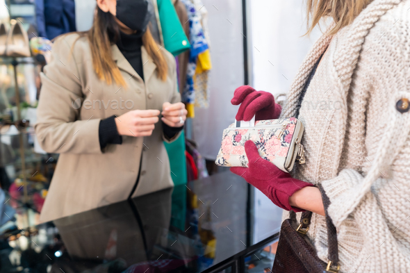 Employee with masks in a clothing store handing over clothes to a ...