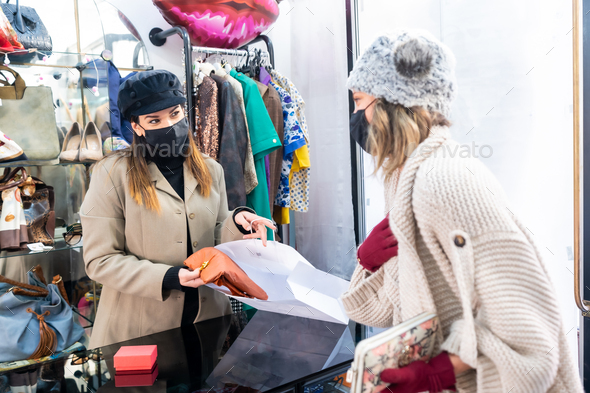 Employee with masks in a clothing store handing over clothes to a ...