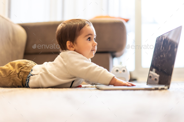 Baby lying on the floor having fun playing on his father's work ...