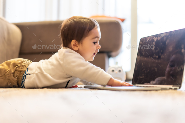 Baby lying on the floor having fun playing on his father's work ...