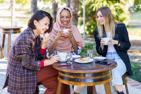 Laughing diverse women having coffee break in outdoor cafe Stock Photo ...