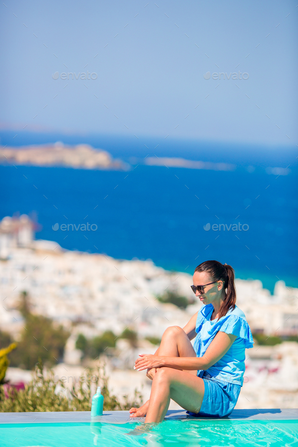 Slim Woman Applying Sunscreen On Her Legs Sitting On The Edge Of Pool