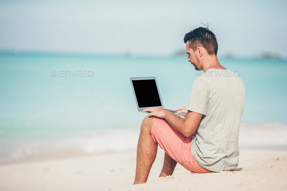 Young man sitting on sand with laptop on tropical caribbean beach. Man ...