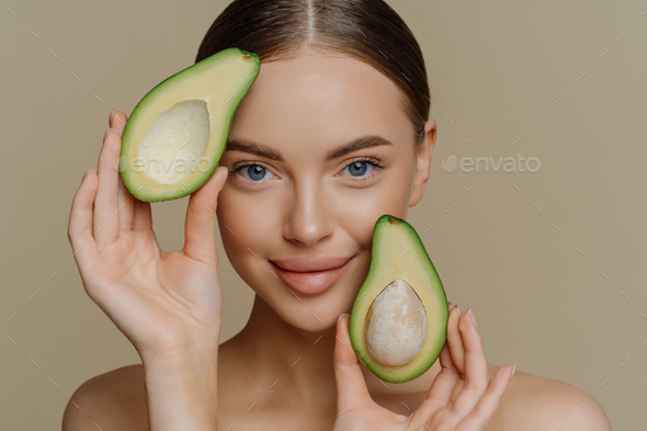 Woman holds halves of avocado near face chooses healthy nutrition has ...