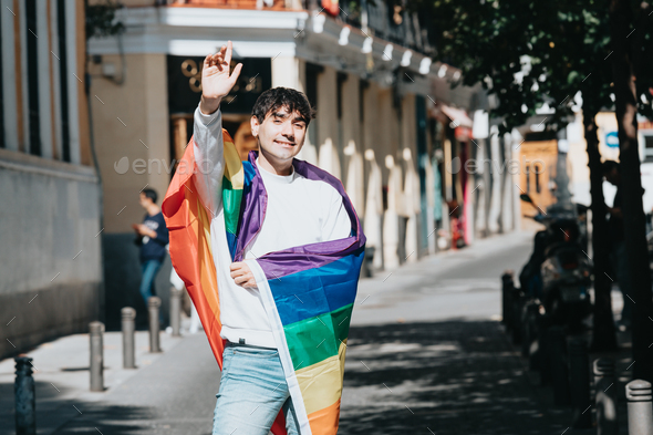Young gay man wrapped in a rainbow flag standing saluting to camera in ...