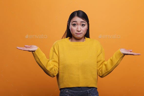 Confused uncertain asian woman shruging unsurely while wearing yellow ...