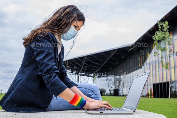 LGBT woman working with laptop, face mask and LGBT bracelet. LGBTQIA ...