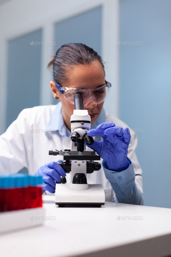 Microbiologist woman looking into medical microscope analyzing virus ...