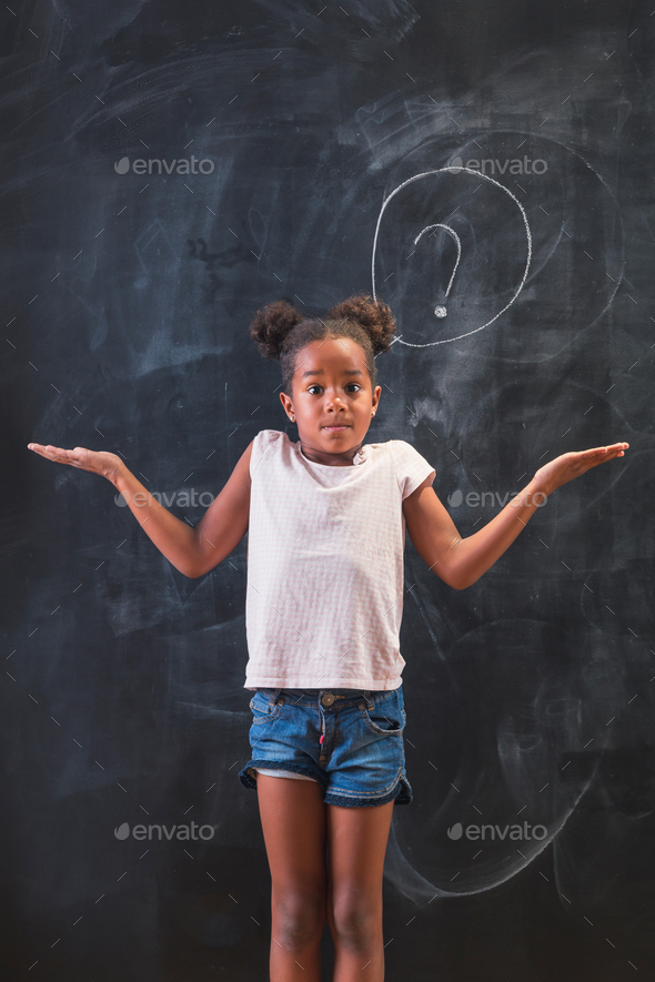Child standing confused in front of a chalkboard, wondering with ...