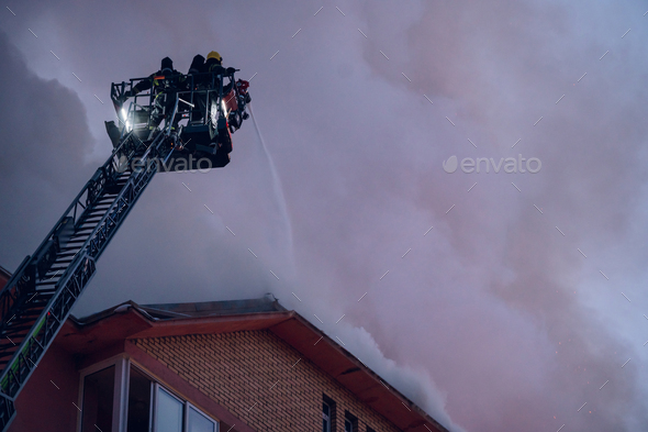 Firefighter on pull-out crane put out a fire in a burning building ...