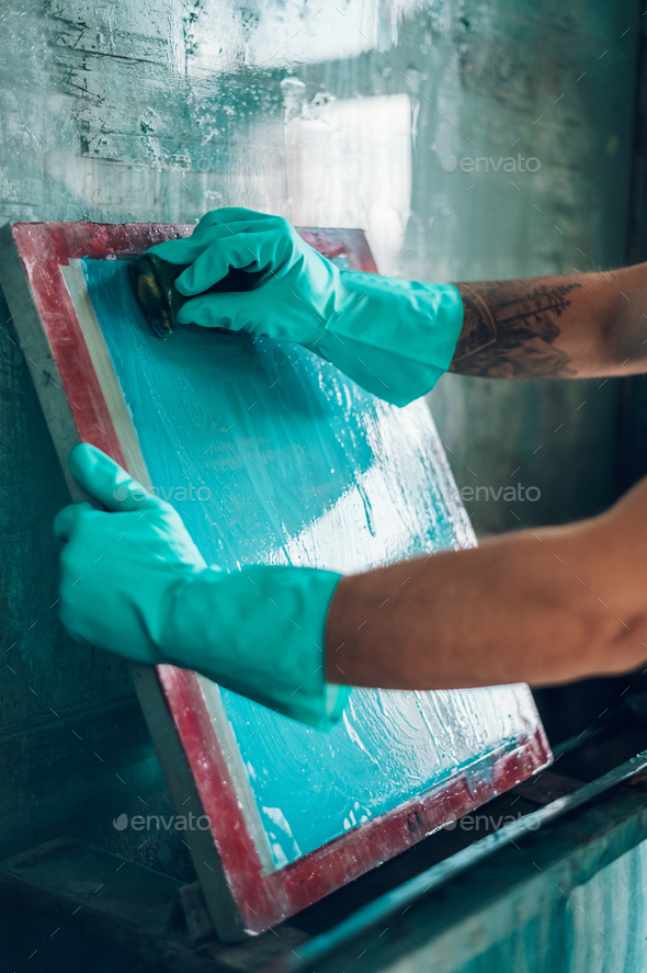 Male worker cleaning screen frame with a sponge in a printing workshop ...