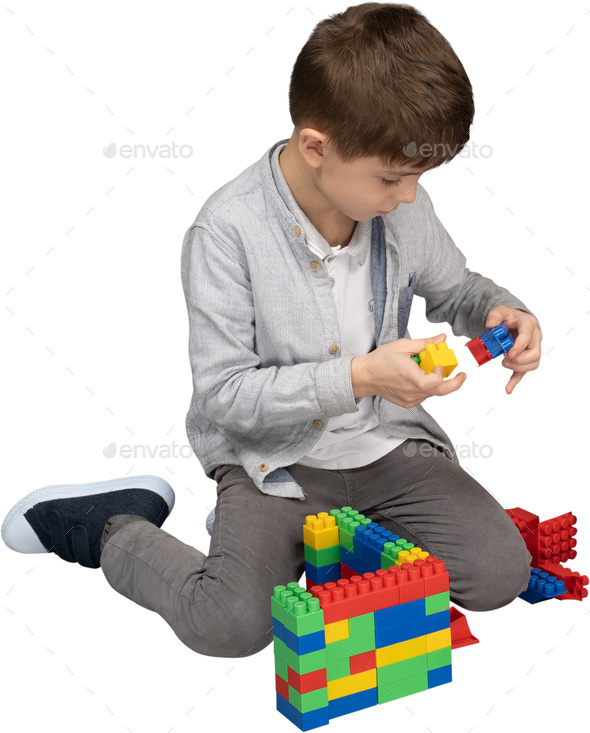 a boy sitting on the floor playing with lego bricks Stock Photo by Icons8