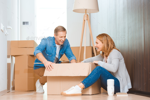cheerful couple sitting on floor and unpacking cardboard box Stock ...