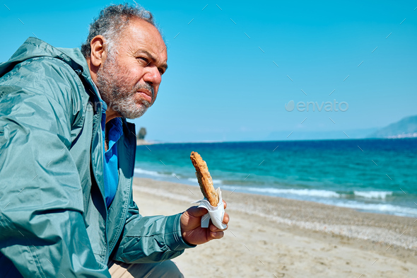 Bearded mature man at spring seaside eating hot palatable panzerotti ...