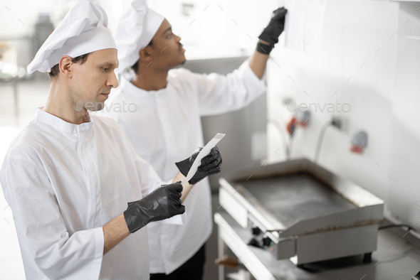 Chefs look on printed checks with orders while cooking in the ...