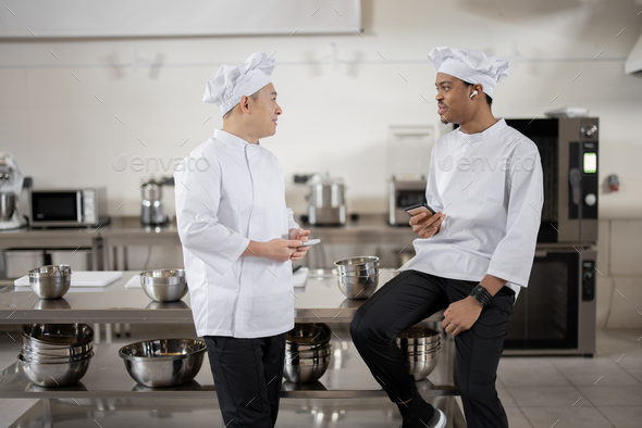 Two multiracial chef cooks talking during a break at the professional ...
