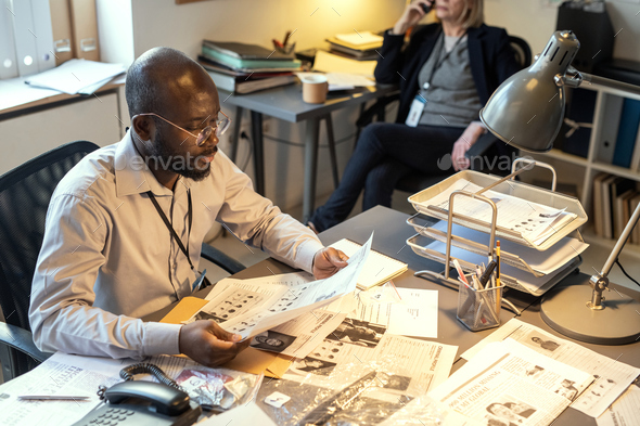 Serious male agent of FBI learning criminal profiles by desk in office ...
