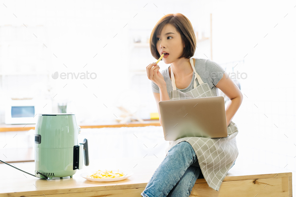 Asian woman using laptop while cooking with Air Fryers and eating ...