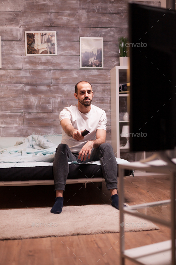 Man sitting on the edge of his bed at night Stock Photo by DC_Studio