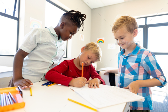 Multiracial elementary schoolboys looking at male classmate writing on ...