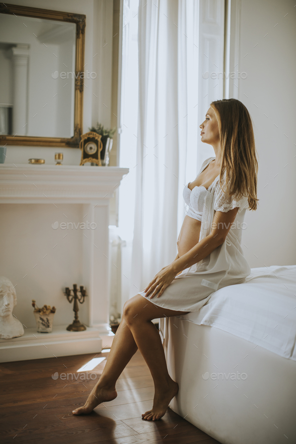 Pregnant Woman Wearing White Lingerie And Posing In The Room Stock
