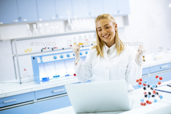 Happy female researcher in white lab coat using laptop while working in ...